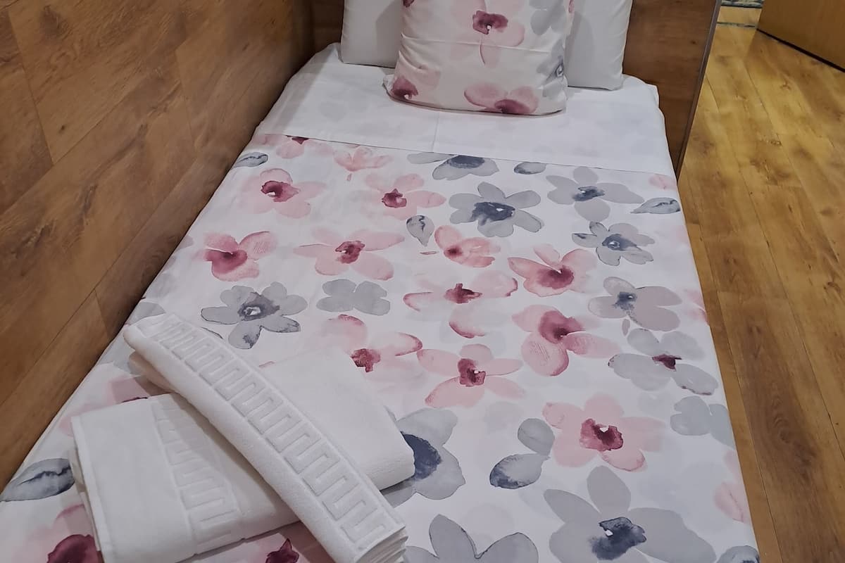 Uma cama pequena com roupa de cama florida, um travesseiro e um cobertor dobrado.