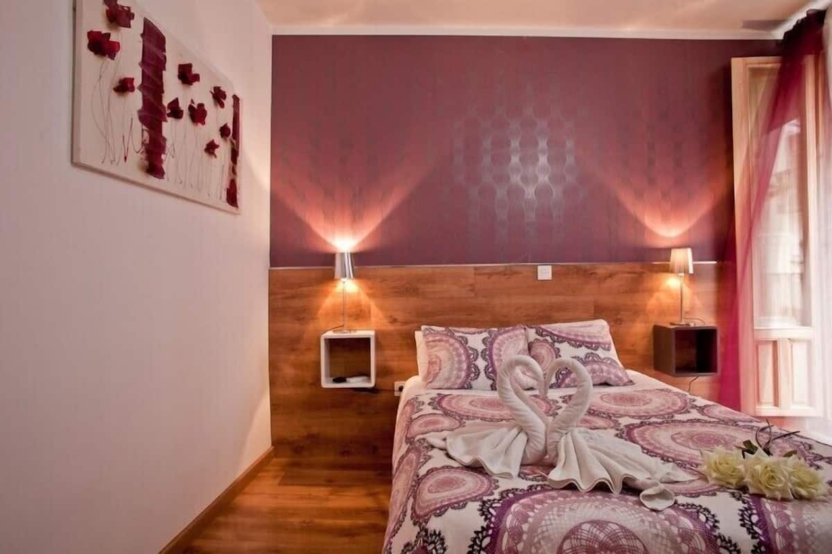 Quarto de hotel com cabeceira de madeira, cama com travesseiro em formato de cisne e arandelas na parede.