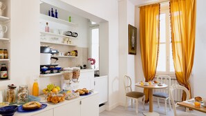 Cozinha iluminada com armários brancos, uma mesa de jantar com cadeiras e uma janela com cortinas amarelas.