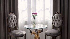 Uma mesa de vidro redonda com um vaso de flores, acompanhada por duas cadeiras estofadas com encostos capitonados.