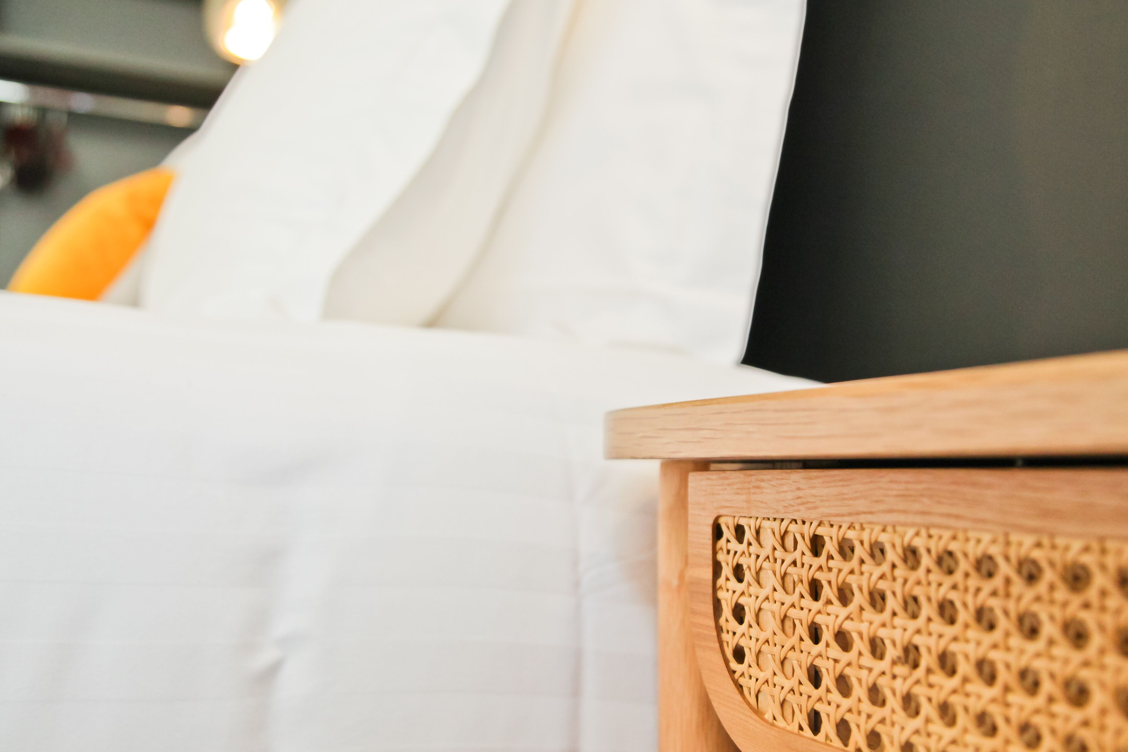 Cama com roupa de cama branca e cabeceira de madeira com encosto trançado.