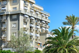Um edifício residencial com vários andares, varandas, uma bandeira e palmeiras.