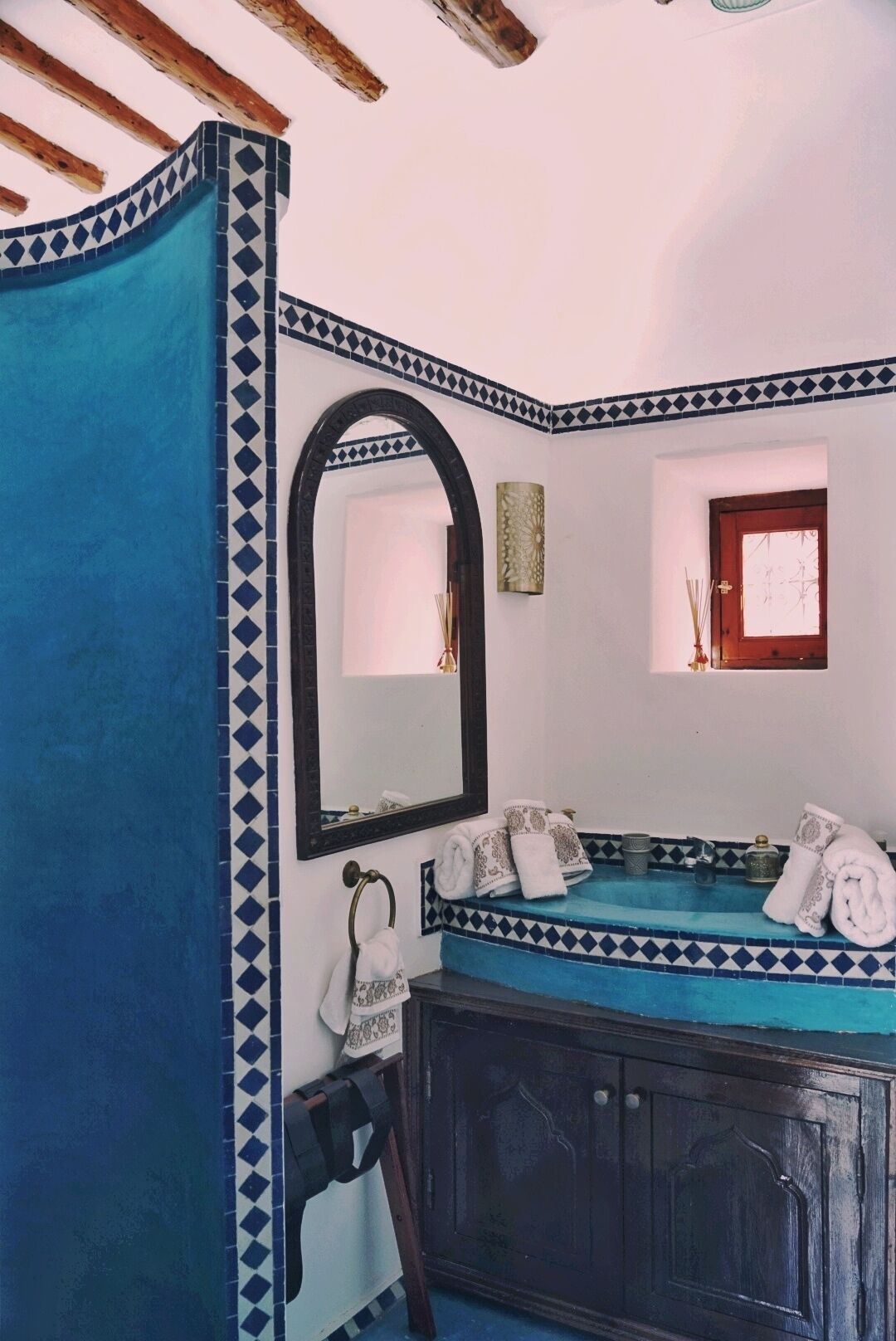 Casa de banho com design de azulejos azul e branco, um espelho grande, uma janela e uma pia com toalhas.