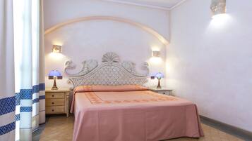 Quarto com cama grande, duas mesas de cabeceira com abajures, cabeceira decorativa e piso ladrilhado em tom claro.