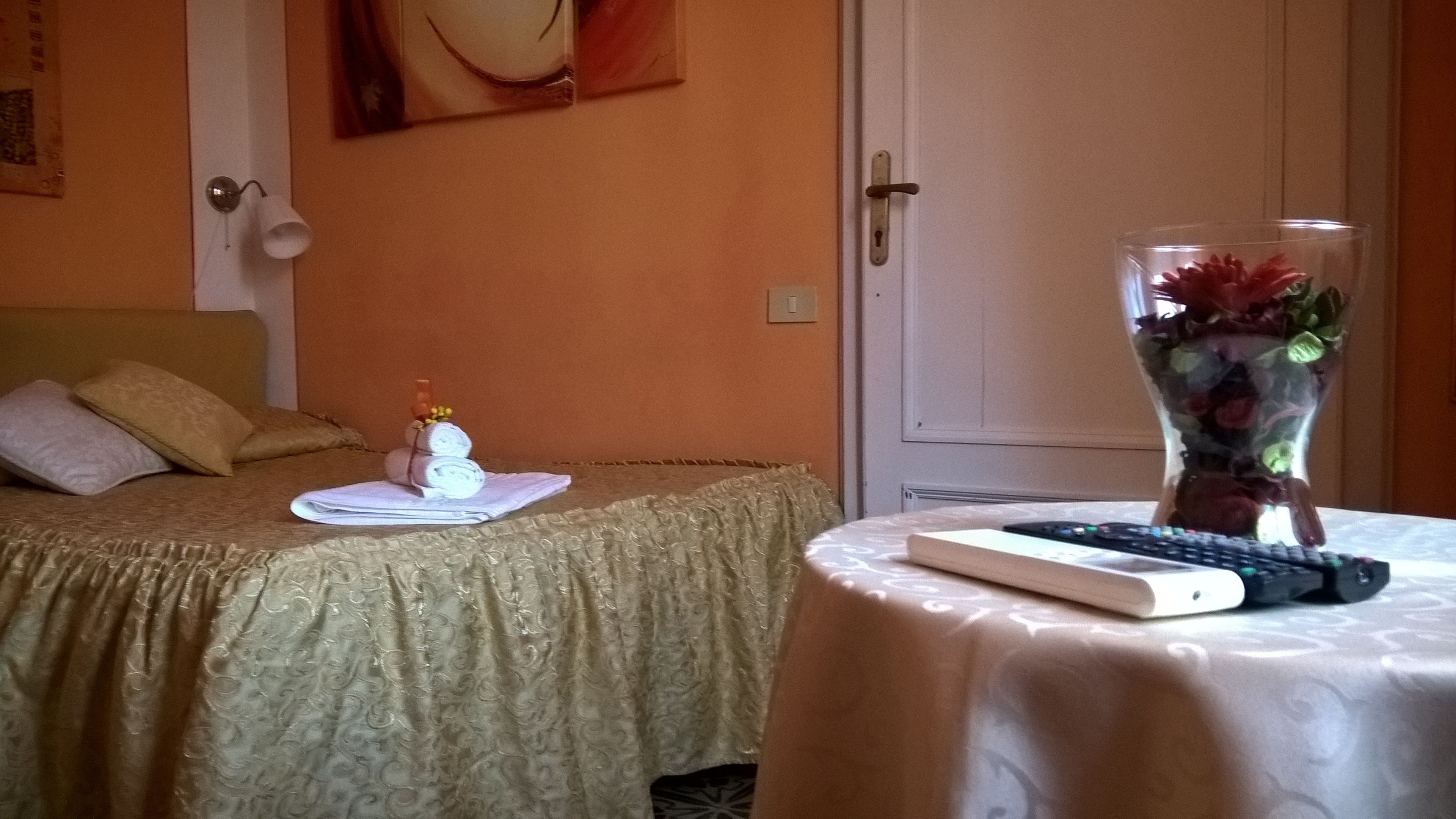 Quarto de hotel com cama, mesa de cabeceira com controle remoto, um vaso com flores e um quadro na parede.