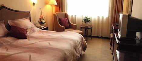 Quarto de hotel com cama grande, uma cadeira, mesa pequena, TV e abajur.