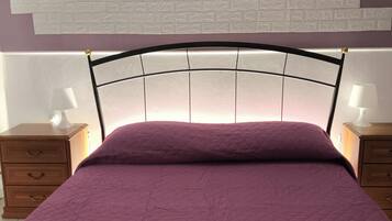 Quarto com cama, duas mesinhas de cabeceira, parede com padrão de tijolos brancos e duas obras de arte emolduradas acima da cama.