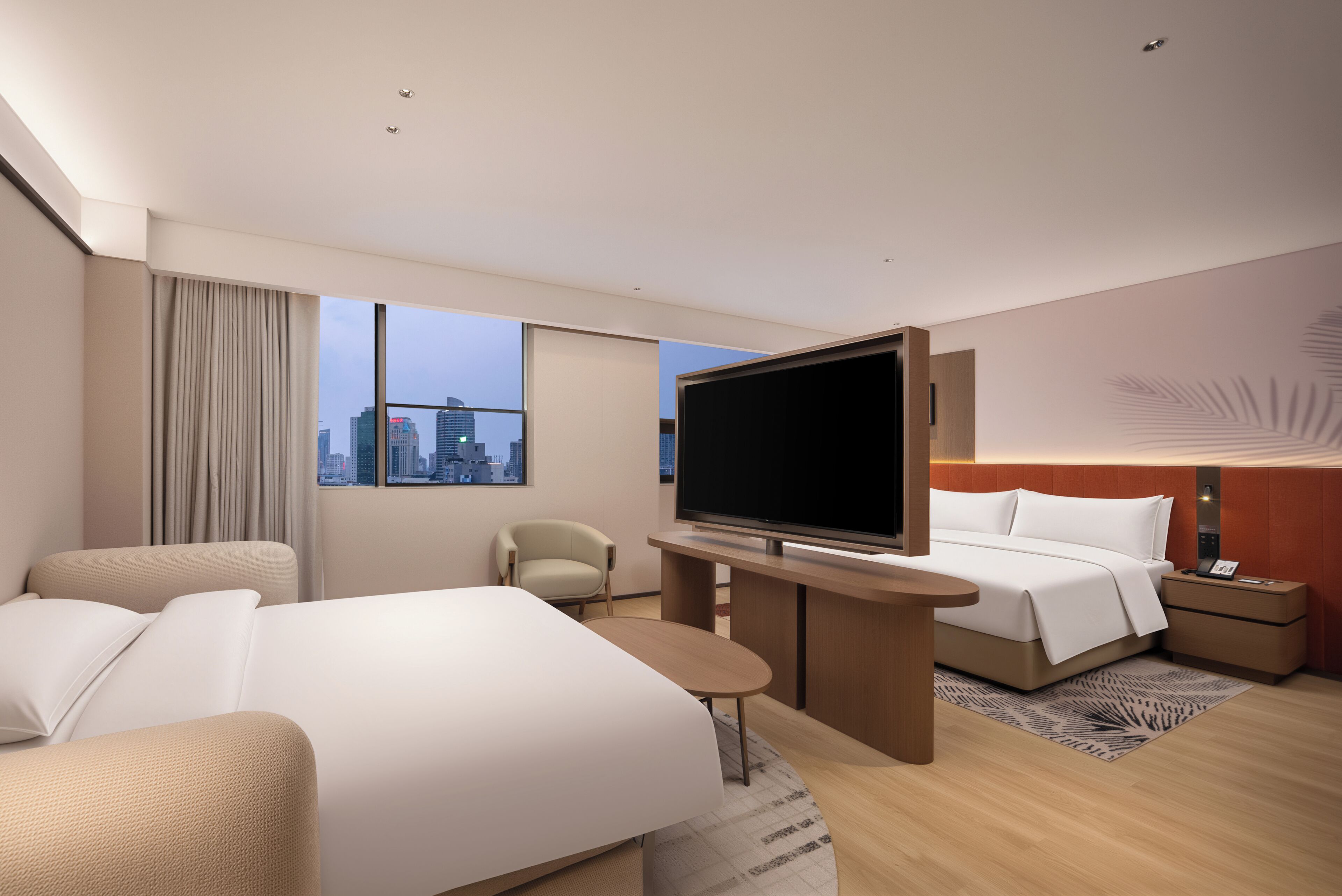 Quarto de hotel com cama, sofá, televisão, escrivaninha e vista para a cidade.
