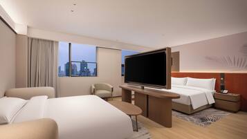Quarto de hotel com cama, sofá, televisão, escrivaninha e vista para a cidade.