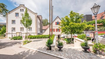 Um hotel com arquitetura europeia tradicional, apresentando um pátio de paralelepípedos, uma área de recepção e uma placa indicando estacionamento.