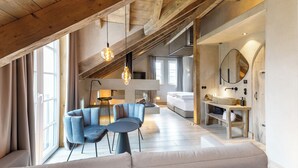 Um amplo quarto no estilo loft, com uma grande janela, uma área de estar aconchegante com sofá e poltronas, e teto de madeira.