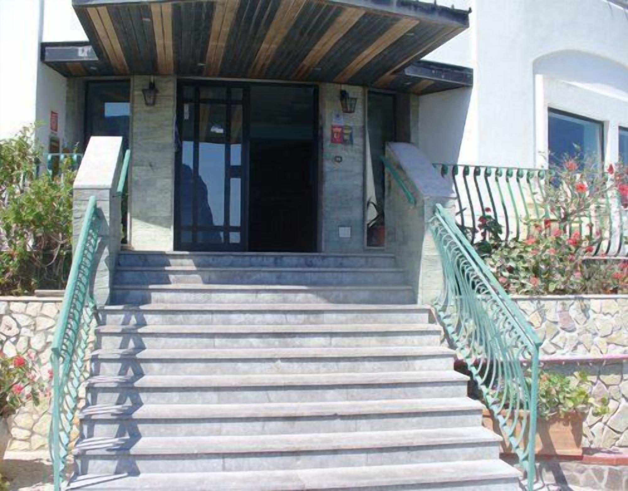 Entrada de um edifício com escadaria de pedra, grade de metal e beiral de madeira.