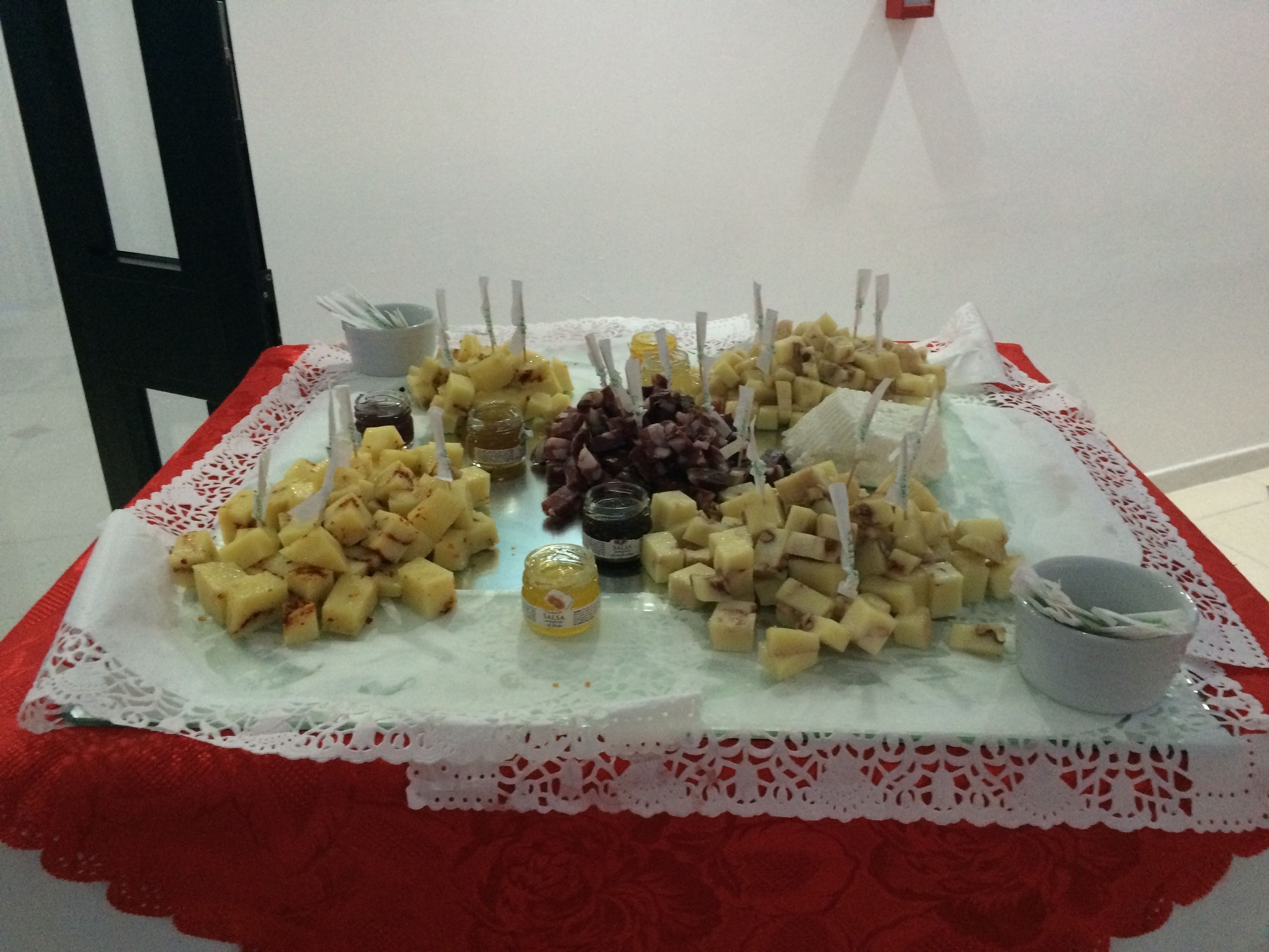 Uma mesa com toalha vermelha e caminho de mesa de renda, exibindo diversos alimentos e acompanhamentos.