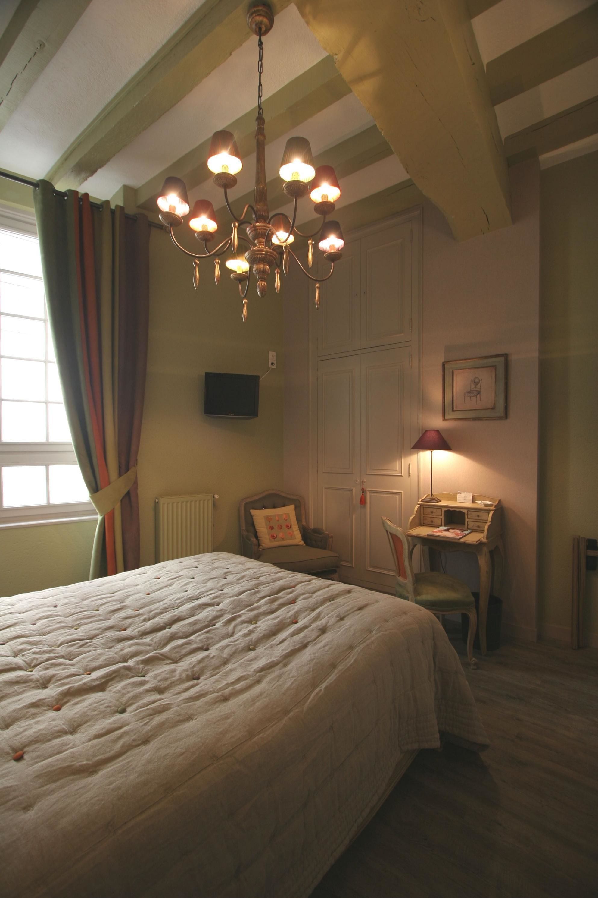 Quarto com uma cama grande, uma escrivaninha com cadeira, televisão na parede e um candelabro.
