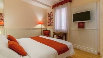 Quarto de hotel com uma cama grande, televisão na parede, escrivaninha com cadeira e janela com cortinas.