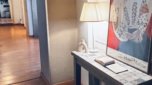 Um corredor com uma luminária, uma obra de arte emoldurada de Henri Matisse e uma pequena mesa com um vaso e um livro.