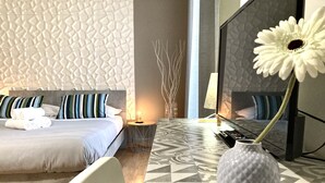 Quarto de hotel moderno com uma cama bem arrumada, um abajur, um vaso com uma flor e um piso estampado.