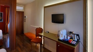 Quarto de hotel com escrivaninha de madeira, televisão na parede, uma cadeira e uma cama.