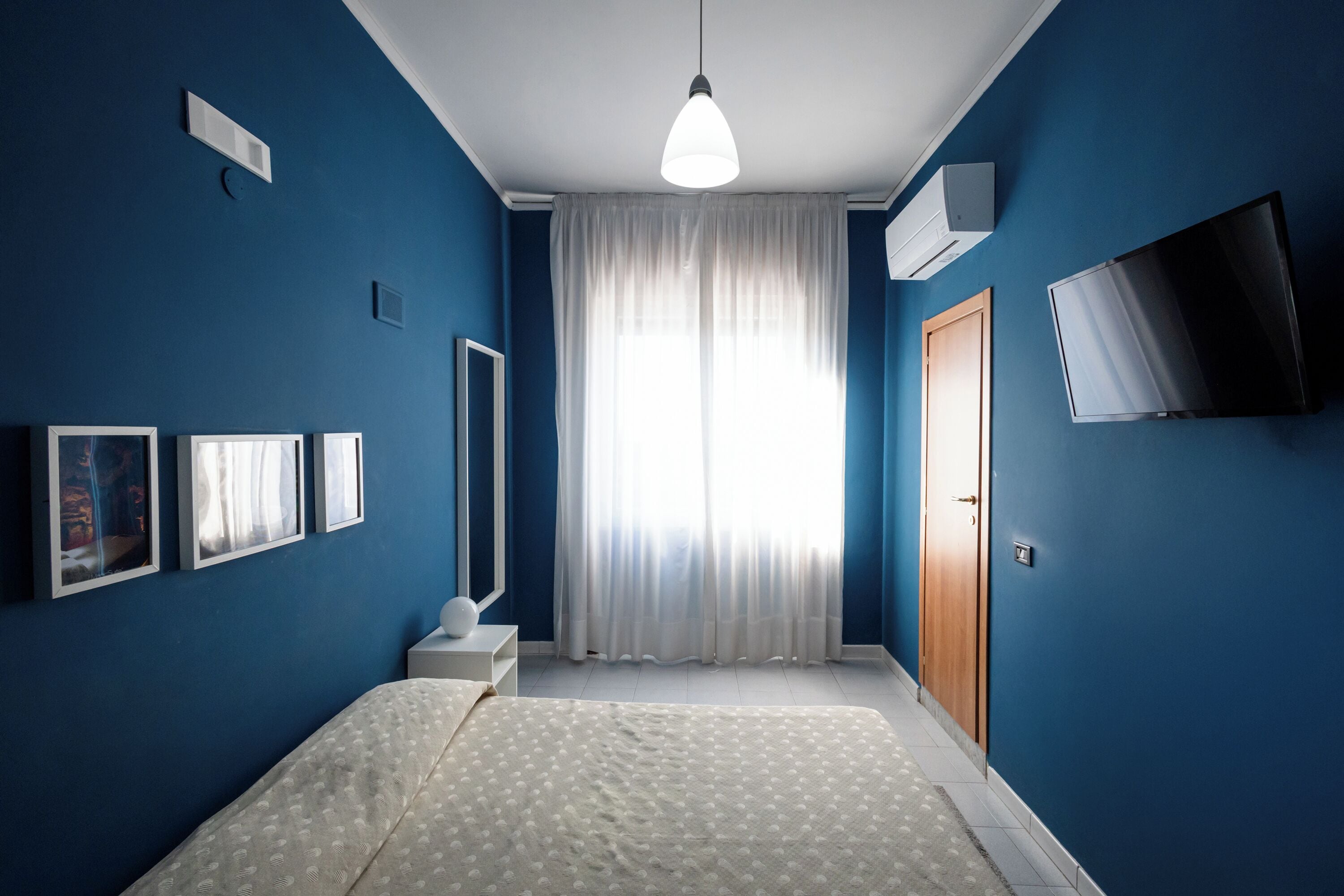 Quarto com cama, televisão, janela com cortinas e porta.