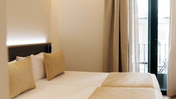 Quarto de hotel com cama, travesseiros, cabeceira e vista para o exterior através de uma janela.