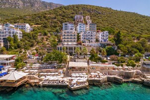 Uma cidade costeira com um porto de iates, águas turquesa cristalinas e edifícios com varandas com vista para o mar.