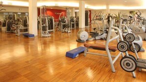 Uma academia espaçosa com diversos equipamentos de cardio, aparelhos de musculação e piso de madeira.