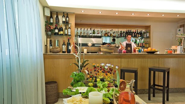 Uma área de bar com diversos tipos de garrafas, um balcão e uma seleção de frutas e legumes.