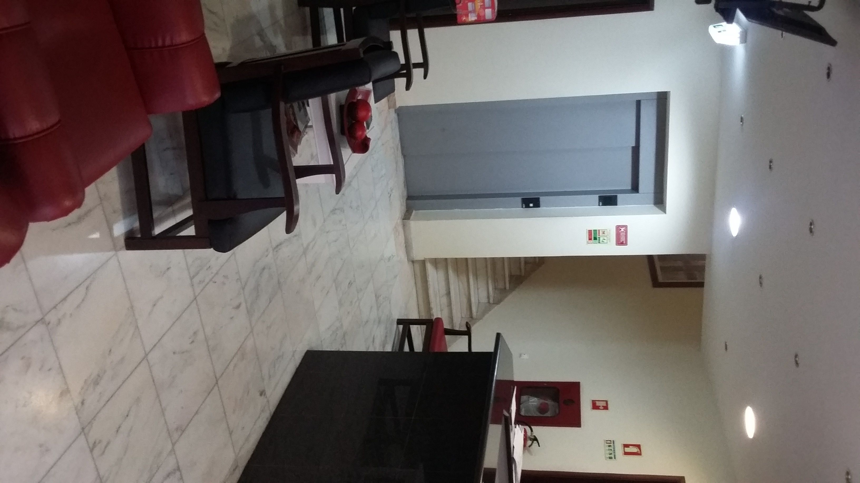 Um hall de hotel com piso de mármore, assentos vermelhos, um balcão de recepção e uma grande janela.