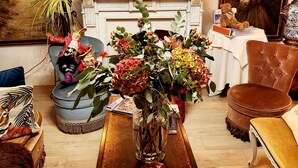 Uma sala de estar acolhedora com uma mesa de centro de madeira, um vaso com flores, um urso de pelúcia e uma lareira com um espelho em cima.