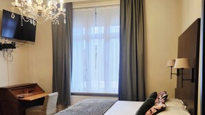 Quarto de hotel com cama, escrivaninha, televisão e lustre.