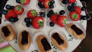 Mesa redonda com padrão floral, exibindo pequenas embalagens de morangos e mirtilos, e doces folhados cobertos de chocolate em copinhos de papel.