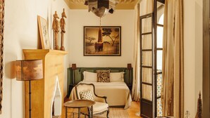 Um quarto com cama, uma cadeira, uma mesa, um abajur e um quadro na parede.
