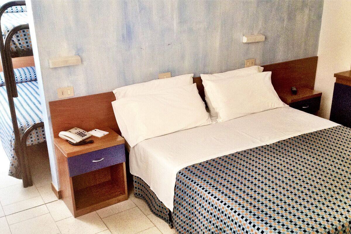 Quarto de hotel com uma cama, mesa de cabeceira e um telefone, e um cobreleite estampado.
