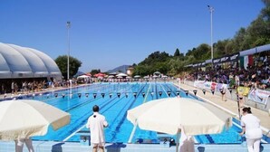 Uma piscina com pistas de natação, espectadores e guarda-sóis.