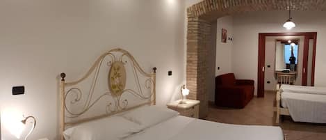 Um quarto com uma cama, mesas de cabeceira, uma cadeira vermelha e um arco que dá para outro cômodo.