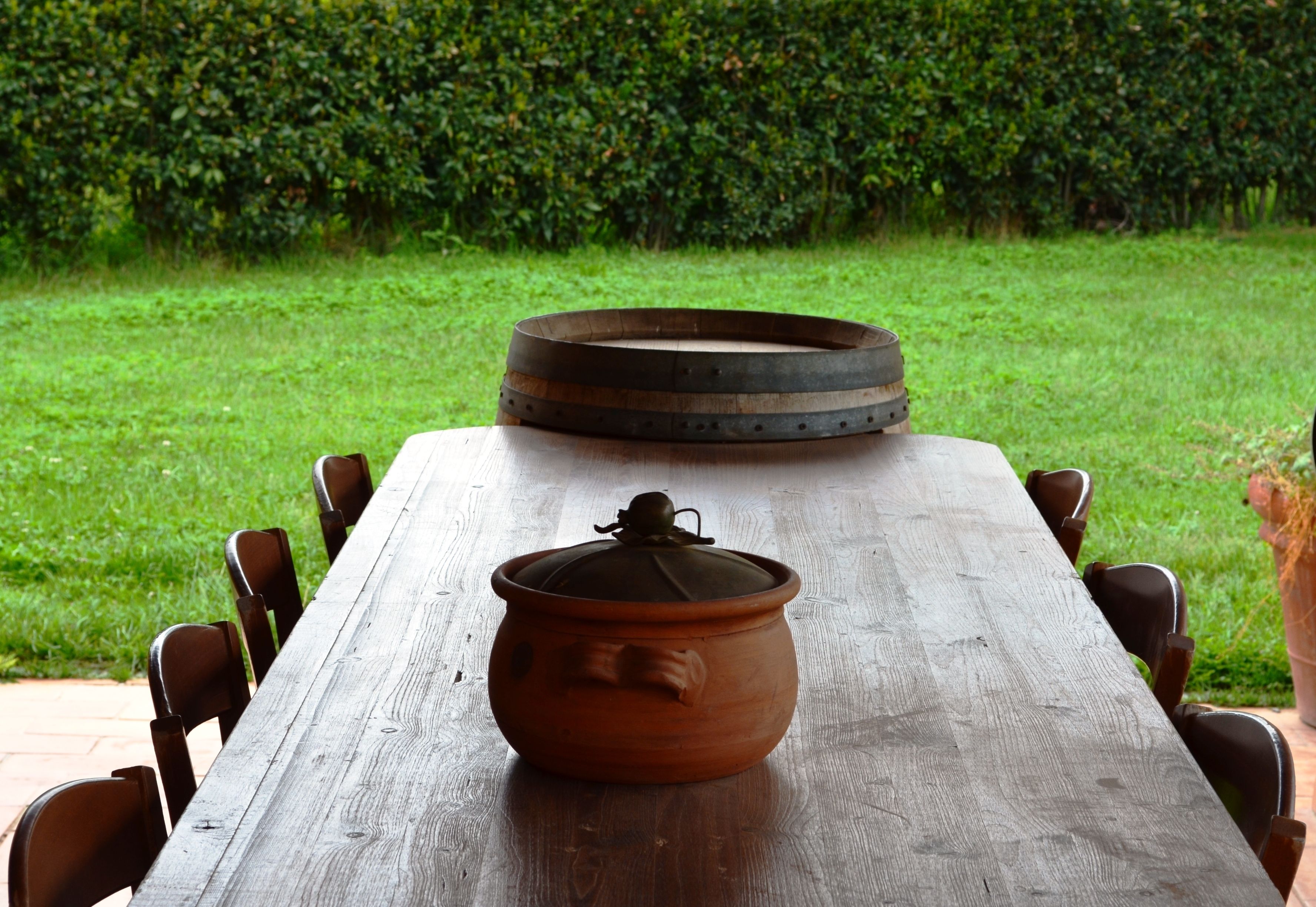 Uma mesa de madeira com cadeiras, uma panela de barro e uma panela de metal sobre ela.