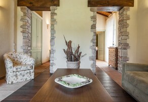 Um quarto com mesa de madeira, pilares de pedra, poltrona estampada e um sofá.