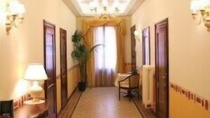 Um corredor de hotel com piso xadrez, arandelas e um candelabro.