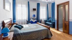 Quarto de hotel com cama, escrivaninha, poltrona, sofá, candelabro e porta deslizante.