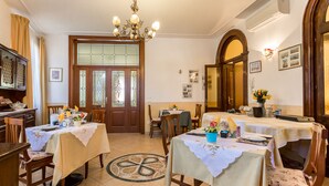 Uma sala de jantar com duas mesas preparadas para refeições, um candelabro e uma grande porta de madeira com painéis de vidro.