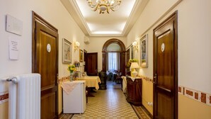 Um corredor de hotel com piso xadrez, portas de madeira, um candelabro e uma mesa com um vaso de flores.