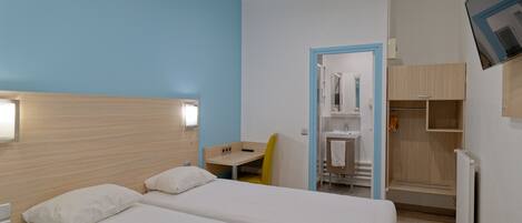 Quarto de hotel com duas camas, uma escrivaninha, uma cadeira, banheiro e televisão presa na parede.