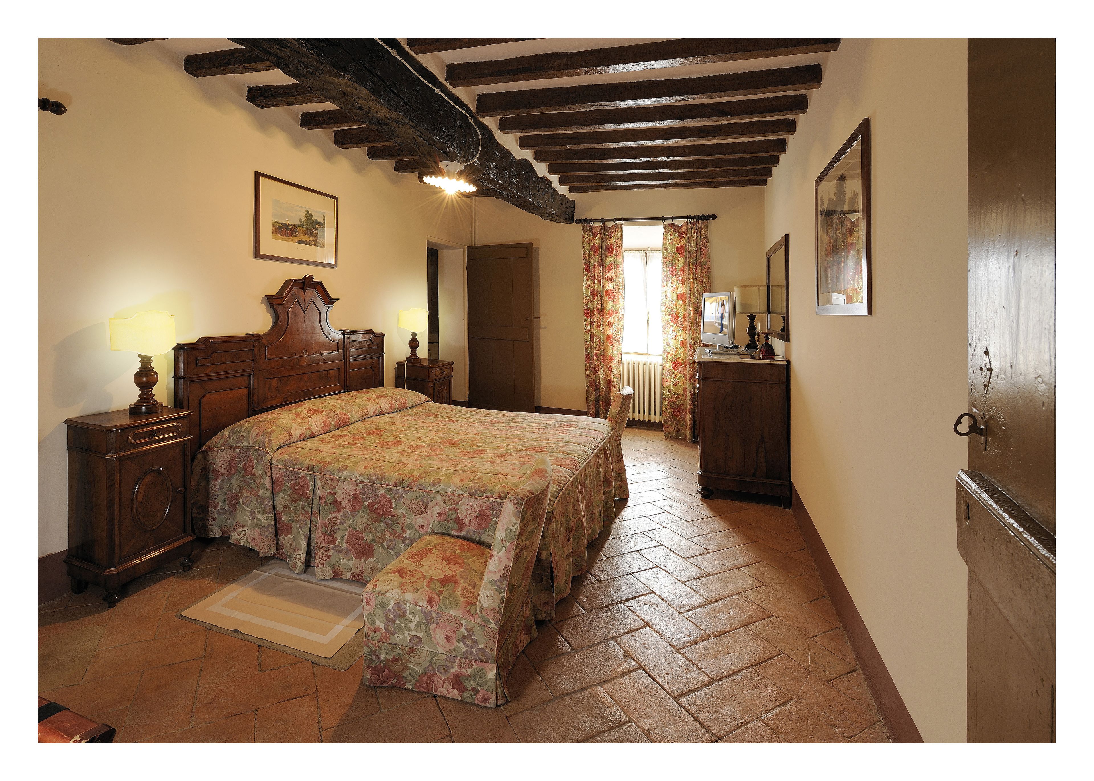 Quarto com cama de madeira, mesa de cabeceira, cômoda e janela com cortinas.