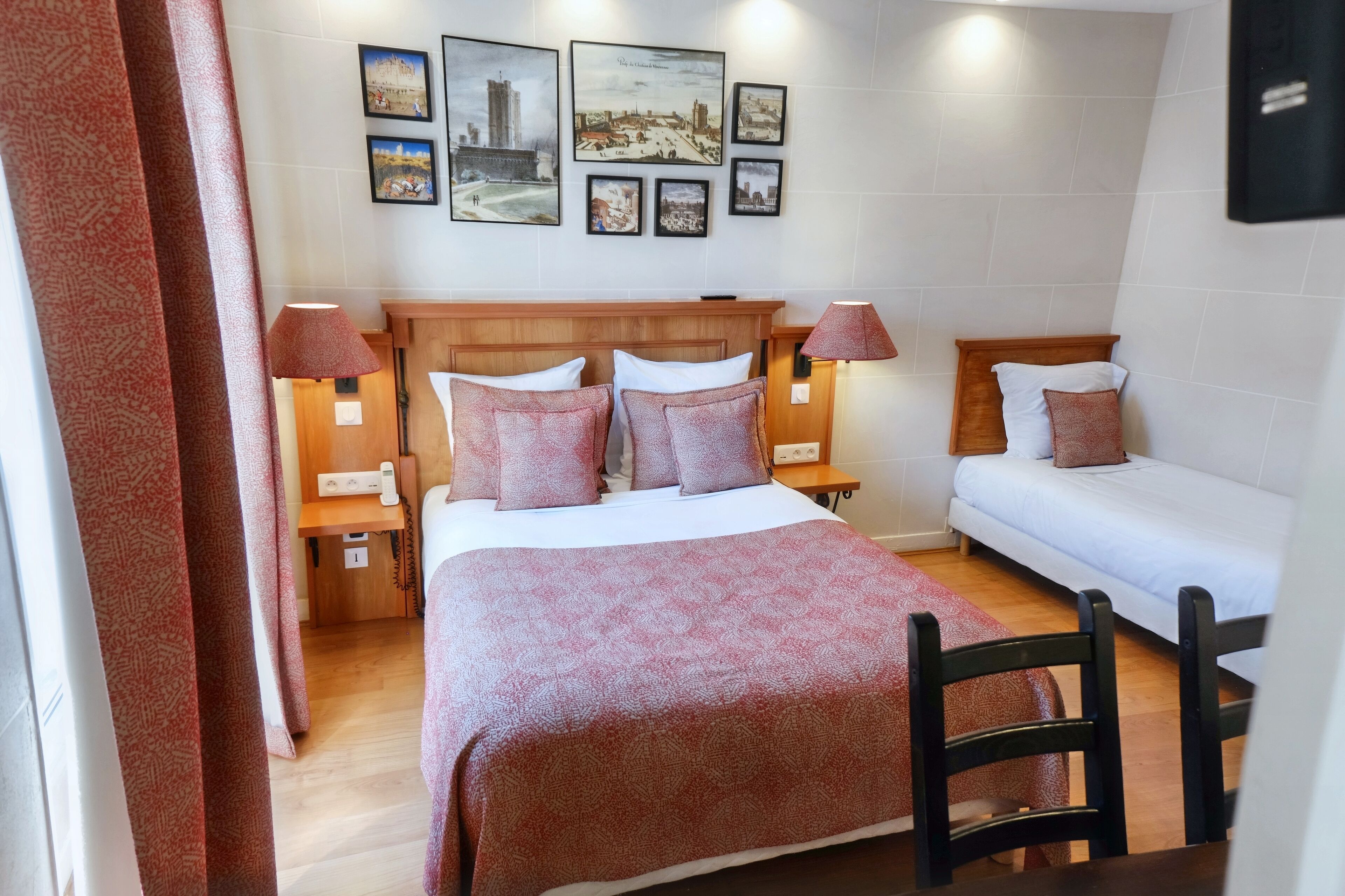 Quarto de hotel com cama, duas mesas de cabeceira com abajures, uma cadeira e um painel de parede com quadros.