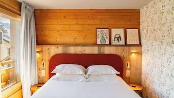 Um quarto com painéis de madeira, uma cama, obras de arte emolduradas e uma janela com cortinas.
