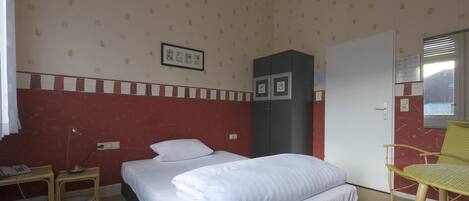 Quarto com cama, guarda-roupa, escrivaninha com luminária e uma cadeira.