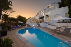 Uma área de piscina moderna com piscina azul cristalina, espreguiçadeiras e guarda-sóis.