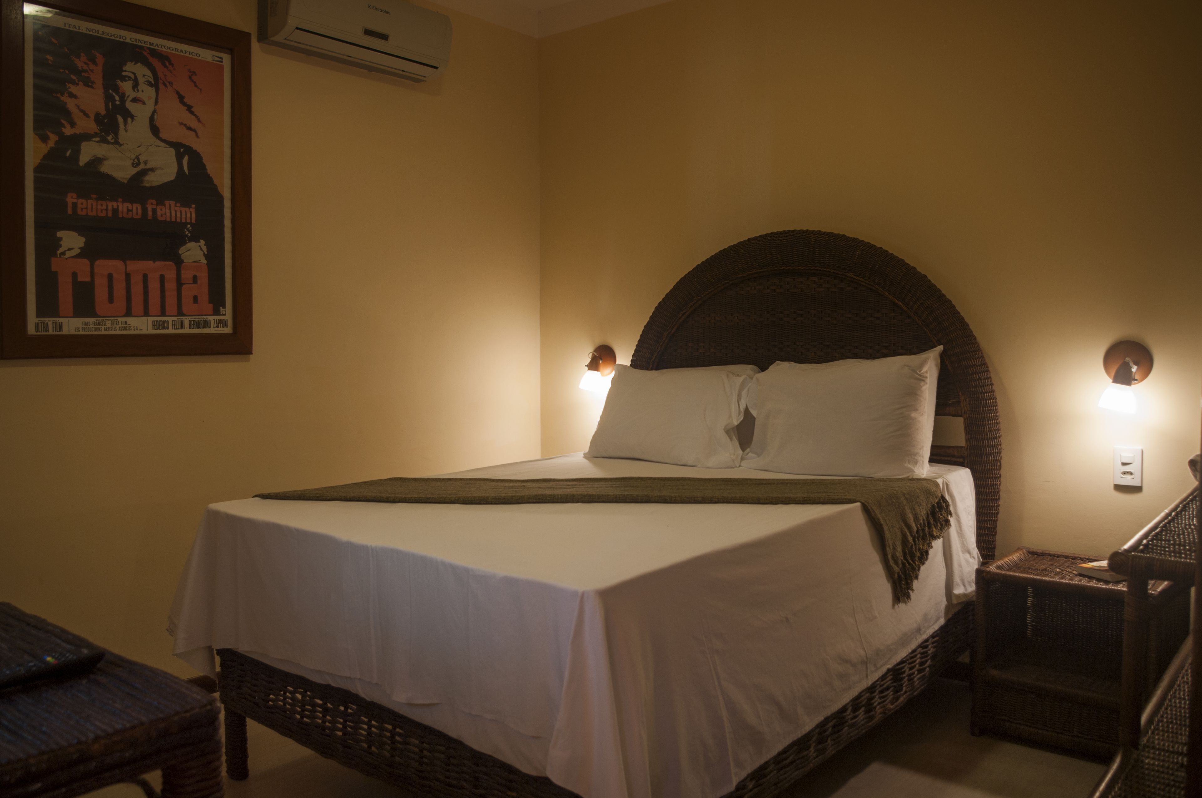 Uma cama bem arrumada com lençóis brancos, uma cabeceira escura e duas luminárias de cabeceira.