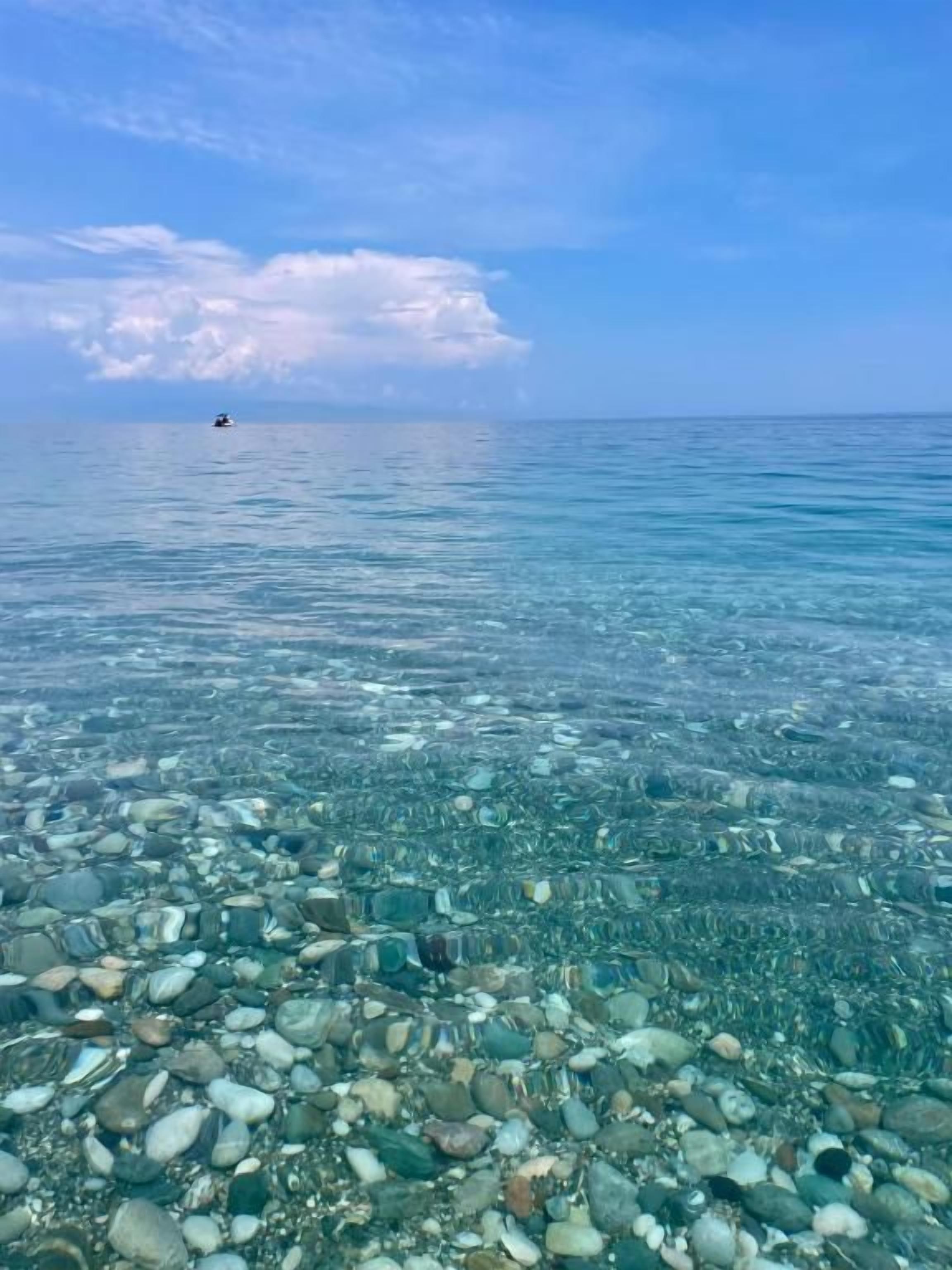Uma vista clara de uma praia com um barco ao longe e um litoral rochoso.