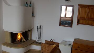 Quarto com lareira, armário de madeira, pequeno frigorífico e janela com persianas.